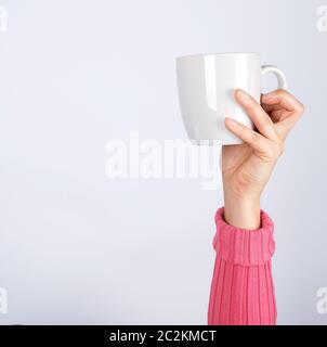 A person holds a white ceramic cup in one hand and a sucrose cube in ...