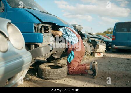 Mechanic stuck head under the hood, car junkyard Stock Photo - Alamy