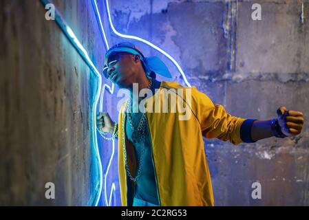 Black rapper in underpass neon light on background. Rap performer in ...