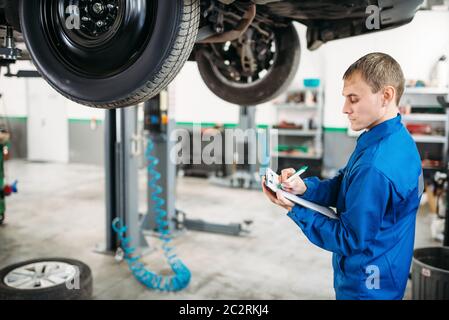 Technician with notebook fills the check list, car on the lift, fixing ...