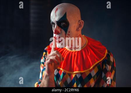 Portrait of mad bloody clown shows the quiet sign, face in blood. Man ...