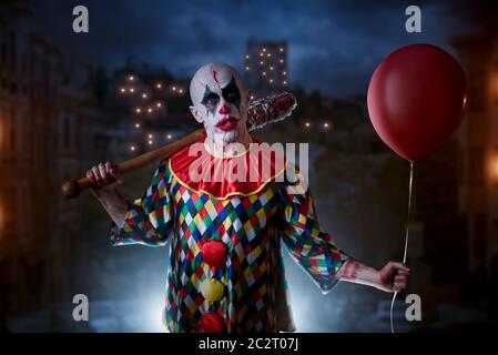Scary bloody clown with baseball bat sitting on the floor, around the ...