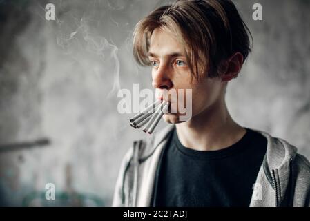 Young junkie with many cigarettes in his mouth reaching his hand ...