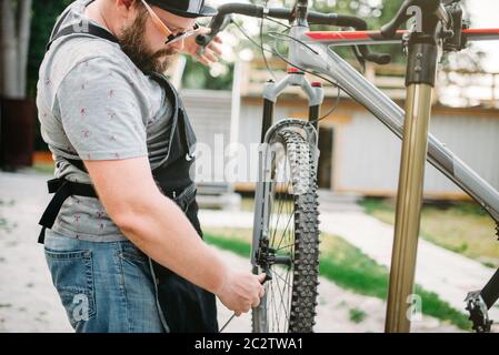 Professional bicycle mechanic in apron adjusts bike. Cycle workshop ...