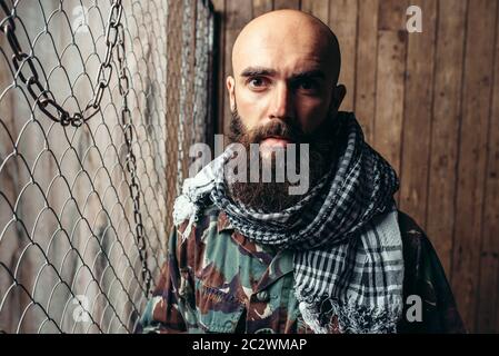 Bearded terrorist in uniform in front of metal grid, male mojahed ...