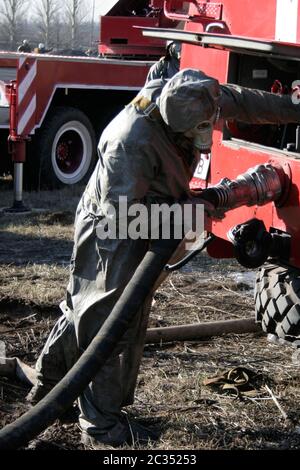 Firefighters in protective suits, gas masks and a hose are getting ...