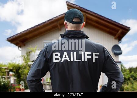 Rear View Of A Male Bailiff Standing With His Hands On Hips At House ...