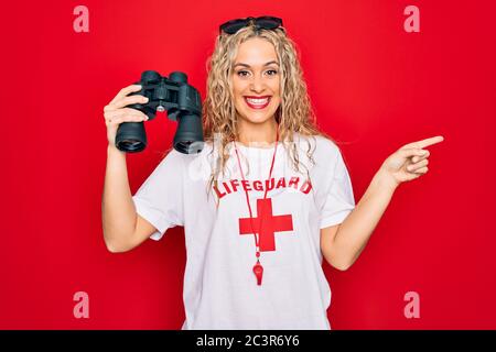 Beautiful lifeguard woman wearing t-shirt with red cross using whistle ...