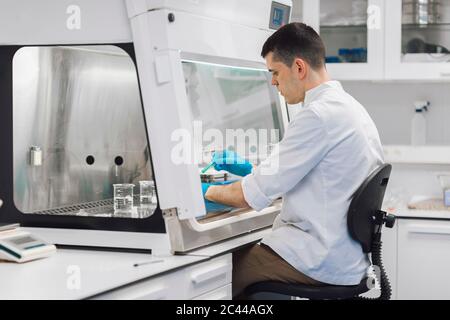 Young hispanic man working at scientist laboratory holding shekels ...