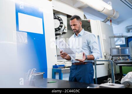 Businessman holding plan and workpiece in factory hall Stock Photo - Alamy