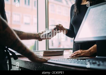 Close up of tattooed bartender standing at counter, handing card reader ...