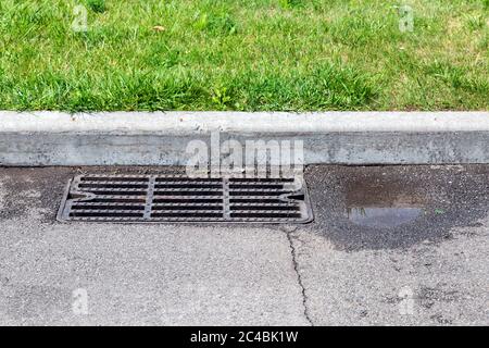 sewer manhole grille on an asphalt road near the curb in the background ...