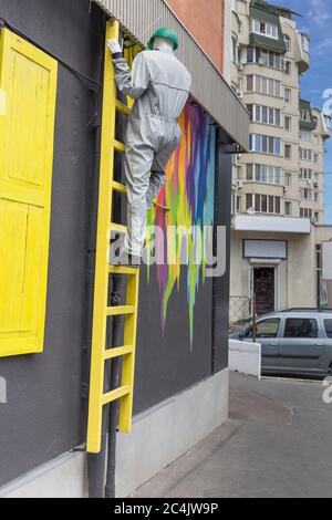 Man decorator coloring wall with yellow color while standing on ladder ...