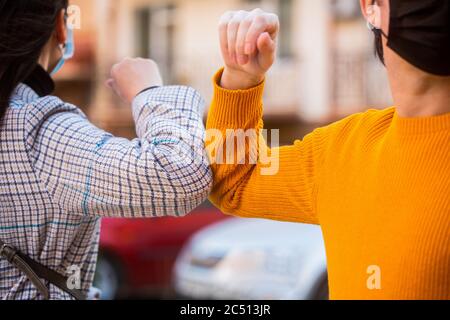 Elbows bump. Friends in protective medical mask on his face greet their ...
