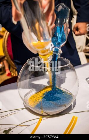 Groom and bride pouring colourful sand into box with glass heart ...