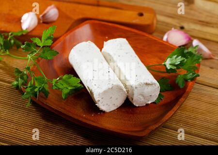 Fresh log shaped goat cheese with garlic and herbs served on plate on ...