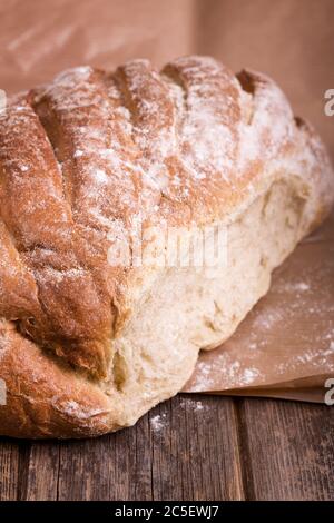 Crusty bloomer loaf, unwrapped from brown paper wrapping, over old wood ...