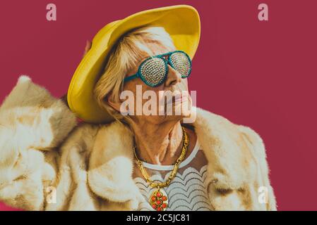 Funny and extravagant senior woman posing on colored background ...