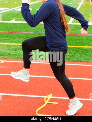 A high school athlete is stepping, running, over yellow mini hurdles during strength and speed ...