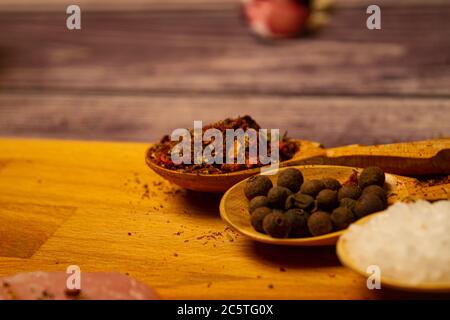 Black allspice, coarse salt and various ground spices in wooden spoons ...