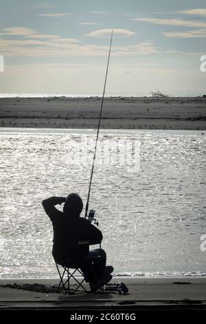 A man is fishing with his seat in the water on "Winter Begins" day of ...