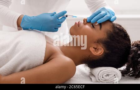 Black lady receiving beauty injections for nose zone at spa, side view ...