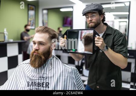 young bearded man getting haircut by a barber while sitting in a chair ...