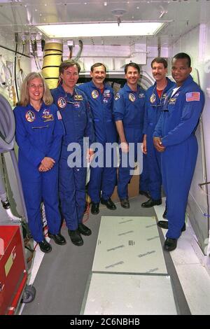 STS-85 Mission Specialist Robert L. Curbeam, Jr. looks down at his glove as a suit technician ...