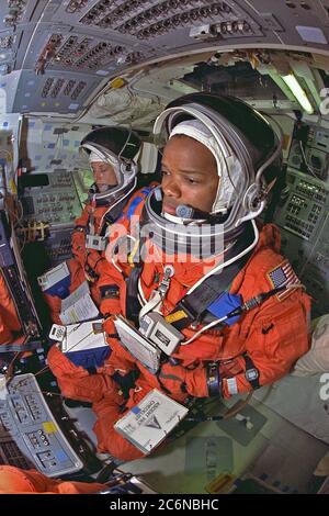 STS-85 Mission Specialist Robert L. Curbeam, Jr. looks down at his glove as a suit technician ...