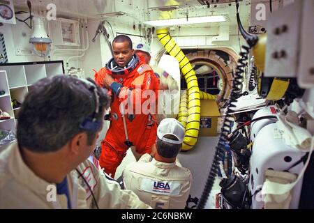 STS-85 Mission Specialist Robert L. Curbeam, Jr. looks down at his glove as a suit technician ...