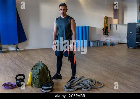 Motivated boot camp instructor stands with gym equipment in gym hall ...