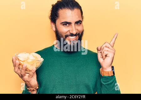 Young arab man holding potato chip smiling happy pointing with hand and ...