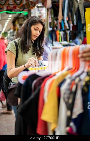 Happy late teen girl looking and buying clothes from outdoor street ...