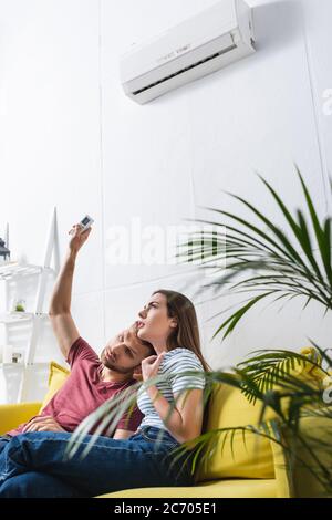 Young man with air conditioner remote control on green background, back ...