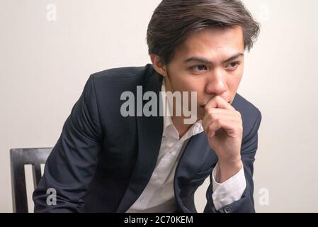 Face of stressed young Filipino businessman in suit having headache ...