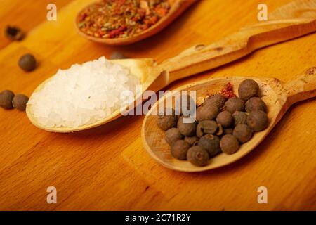 Black allspice, coarse salt and various ground spices in wooden spoons ...
