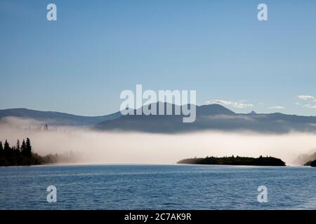 Morning mist drifts across Lake Iliamna, Alaska, with mountains in the ...