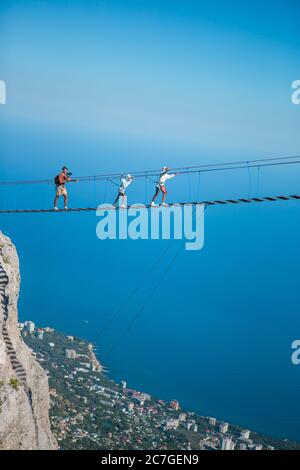 Family crossing the chasm on the rope bridge. Black sea background ...