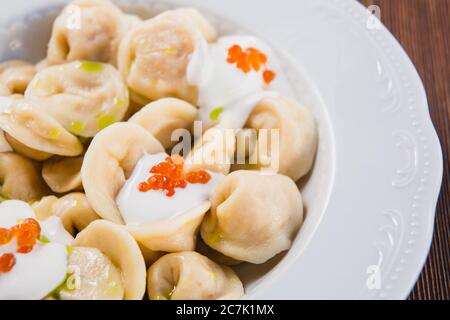 Dumplings Bowl with Red caviar and sour cream on a brown table ...