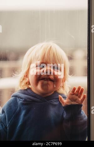 Blonde toddler pushing face up against glass Stock Photo - Alamy