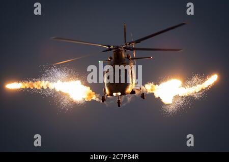 Army helicopter in flight firing off defensive flare decoys at dusk ...