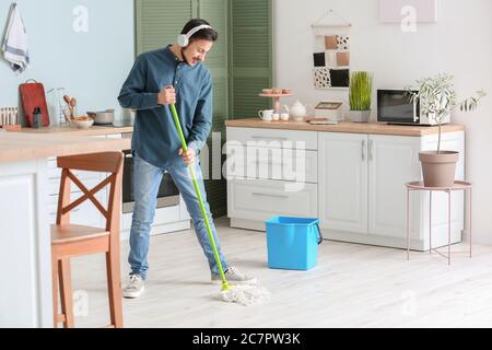 Handsome guy mopping kitchen floor in front of cabinets and countertop ...