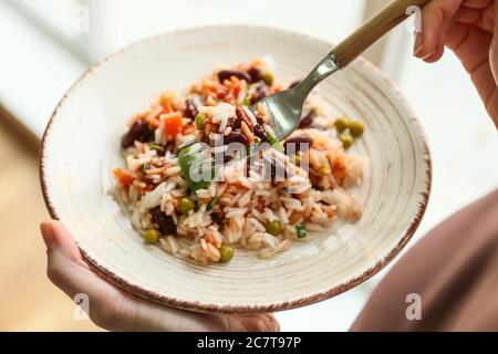 Woman eating tasty rice with beans and vegetables on grey background ...
