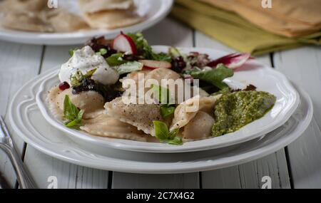 Italian ravioli served with pesto, salad and cream on white plate ...