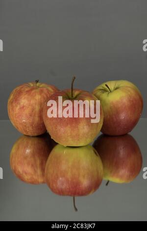 Three red apples on mirroring table on mirror gray background with ...