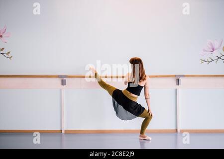 Young woman ballerina stretching and training at barre in dance studio ...
