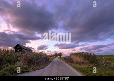 Road passage through dike at sunset under beautiful clouded sky ...