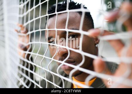 Frustrated young black man behind net outdoors in city, black lives ...