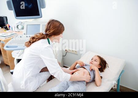 Female doctor examining a little girl's abdomen in her room. Home ...