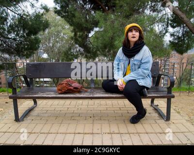 Thoughtful young woman with yellow backpack leaning on blue cracked ...